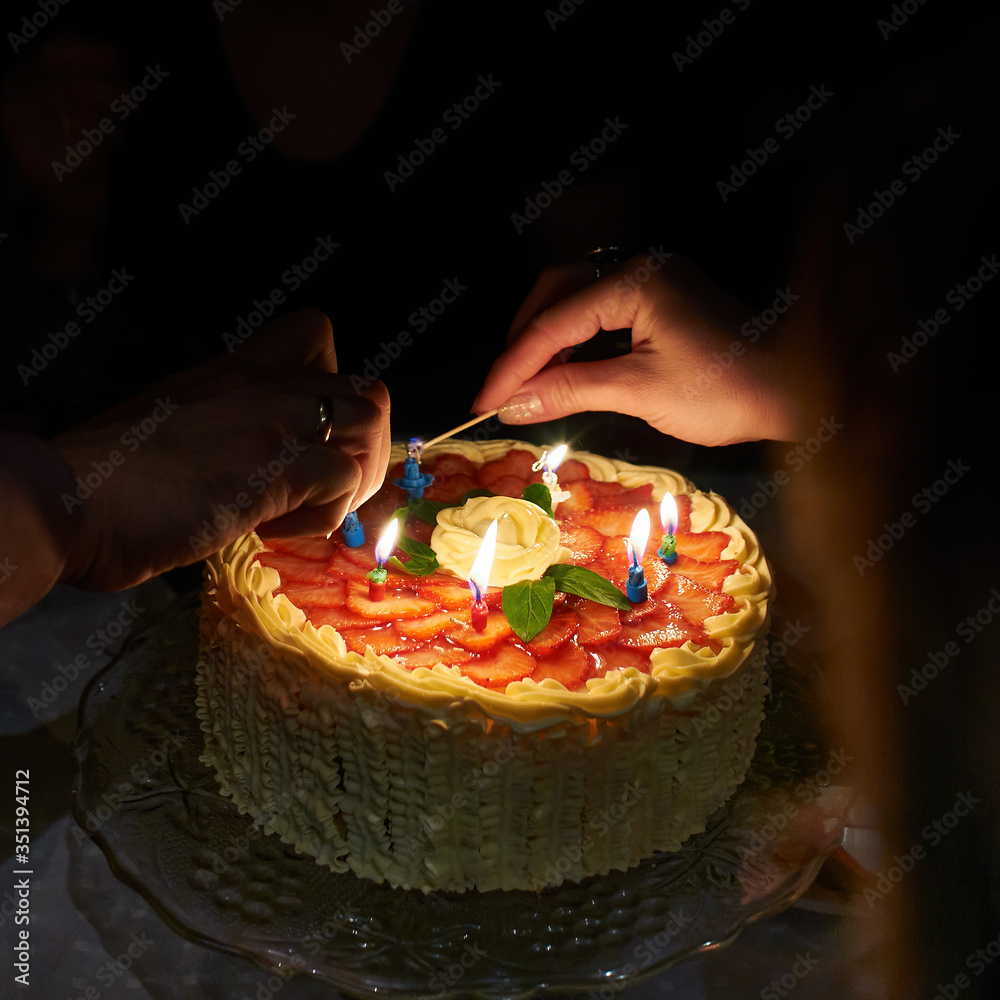 Birthday cake with burning candles. Two hands lighting candles on ...