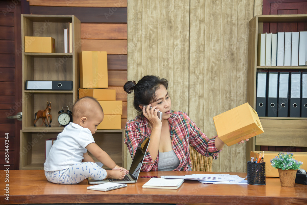 Young mother working on the phone with her daughter sitting on desk ...