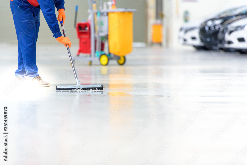 The car mechanic is cleaning, using a mop, rolling water from the epoxy ...