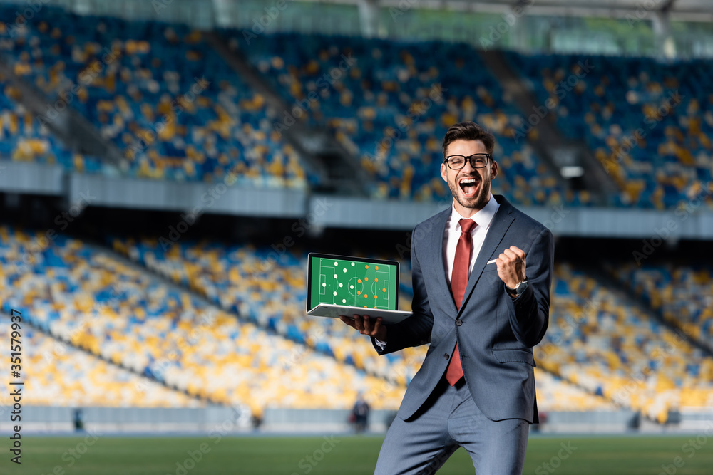 happy young businessman in suit holding laptop with football pitch and ...