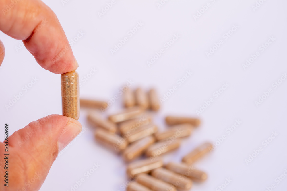 fingers holding herbal capsule, nutritional supplement, vitamin pill ...