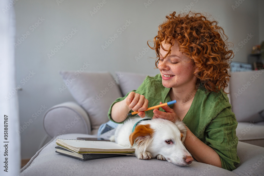 A girl writes in a notebook and plays with a dog. Redhead woman smiling ...