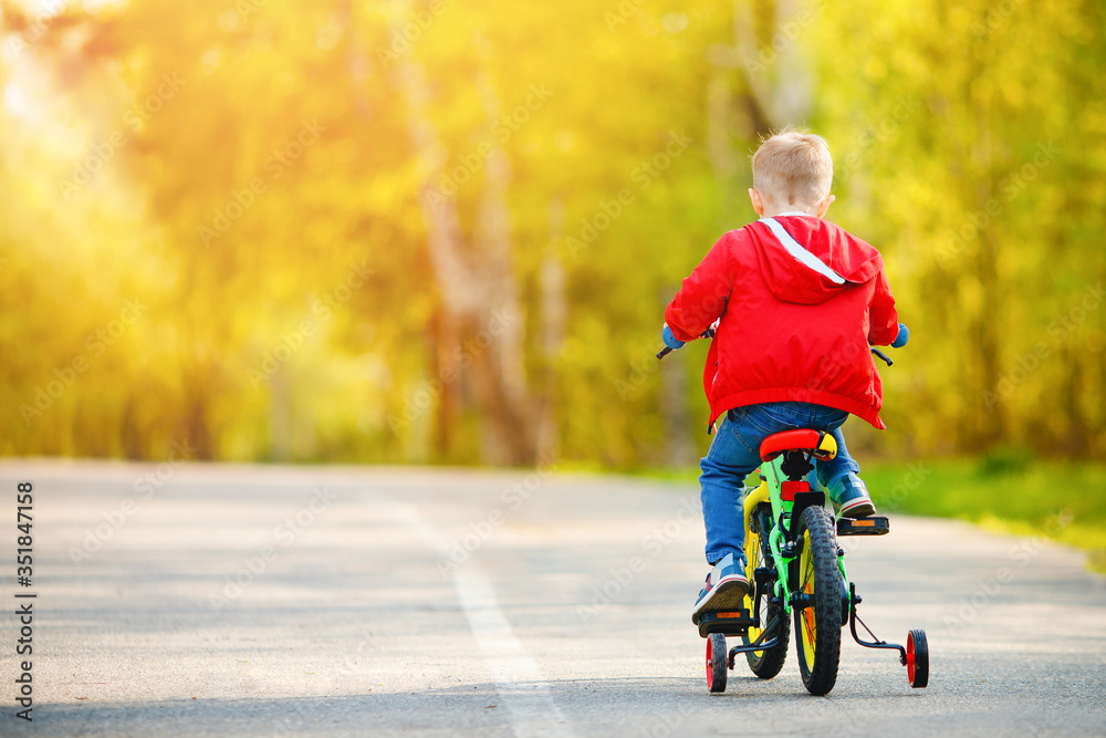 Boy kid training to ride bicycle with supporting wheels on sides, back ...