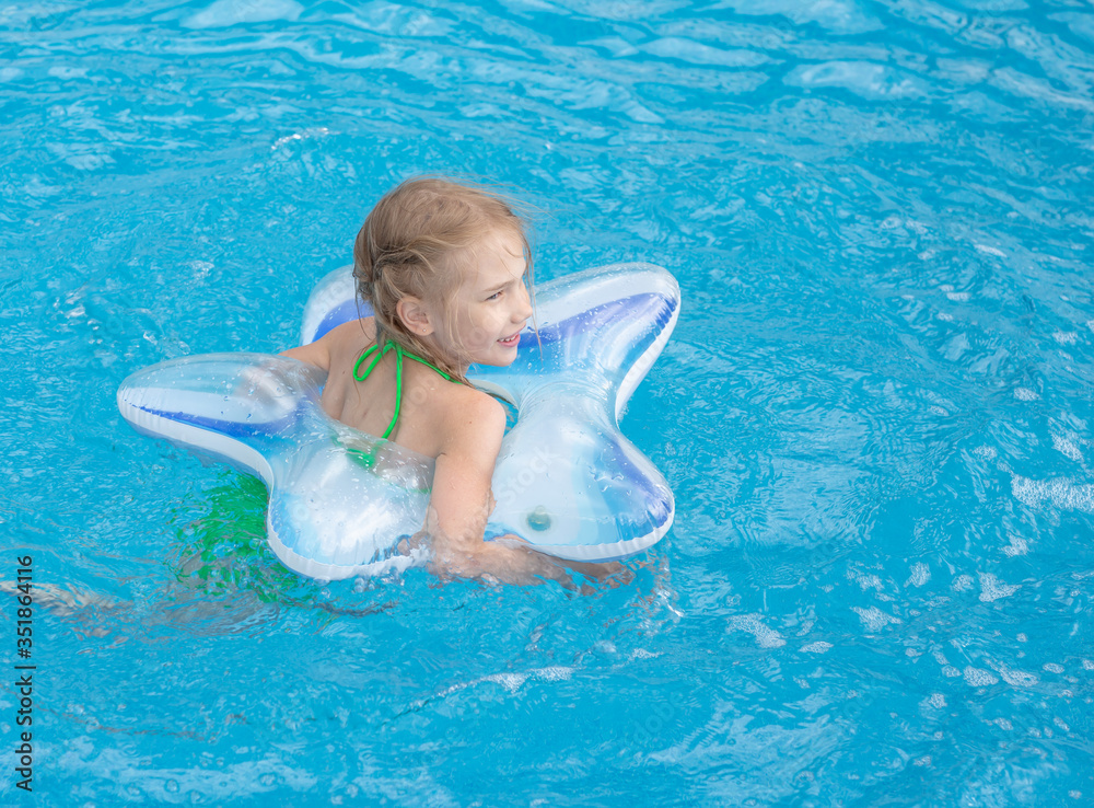 Funny little girl swims in a pool in an transparent life preserver ...