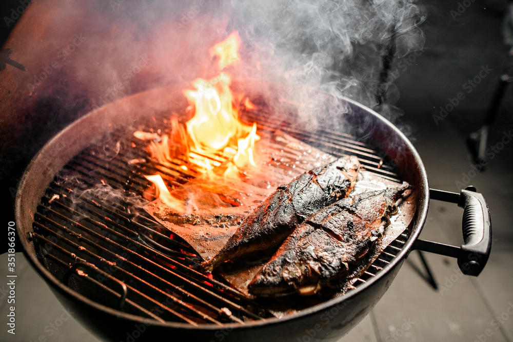 Two fish fried on grill of round barbecue. Stock Photo | Adobe Stock
