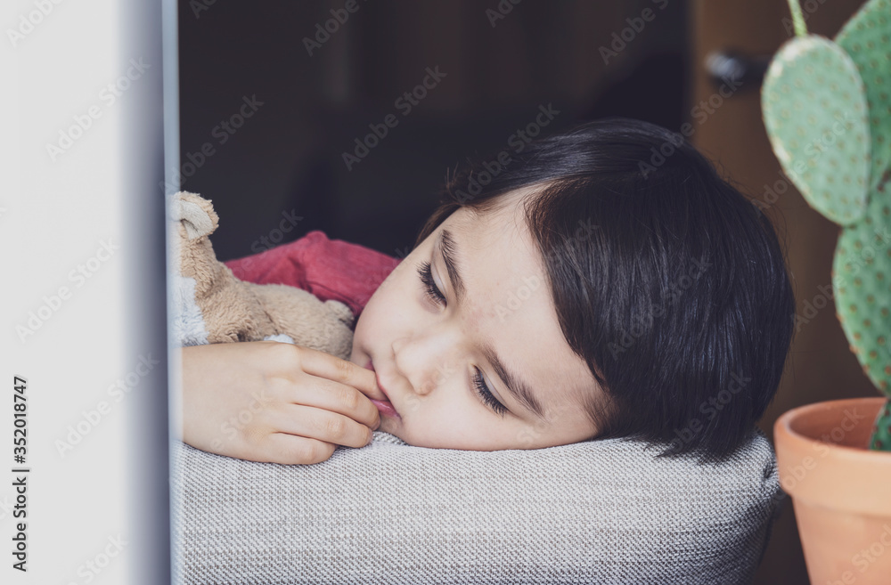 Emotional portrait of caucasian kid sitting next to window with ...