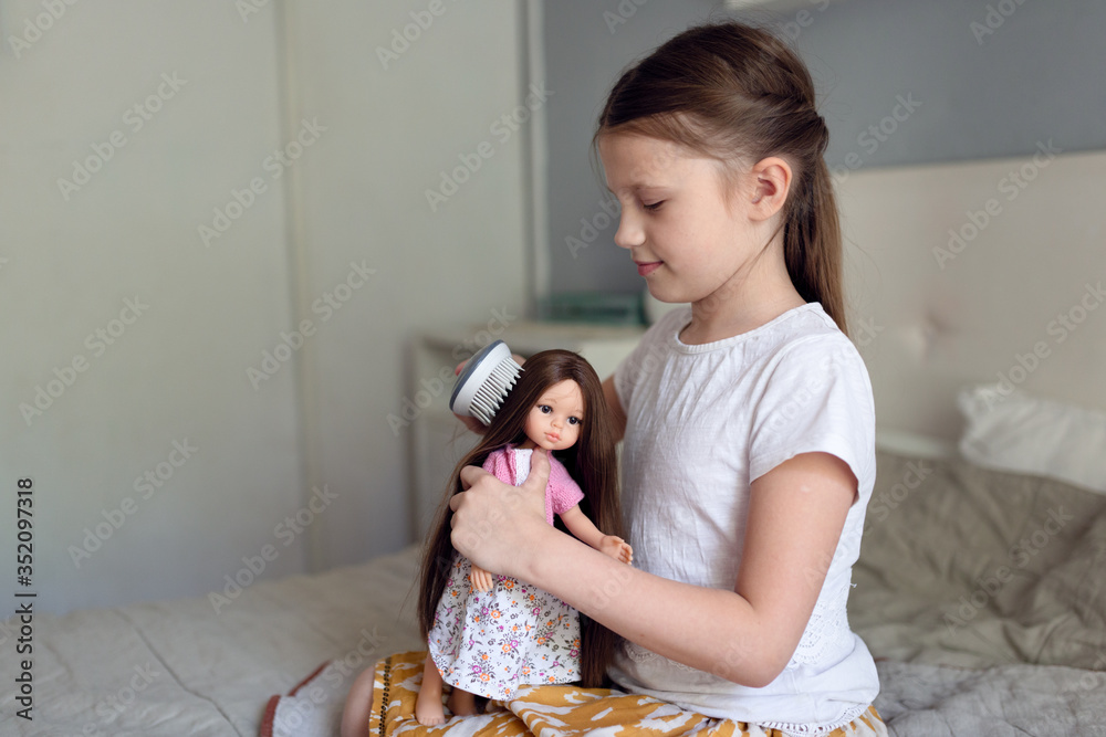 Caucasian girl combing a doll with long hair, a girl playing dolls ...
