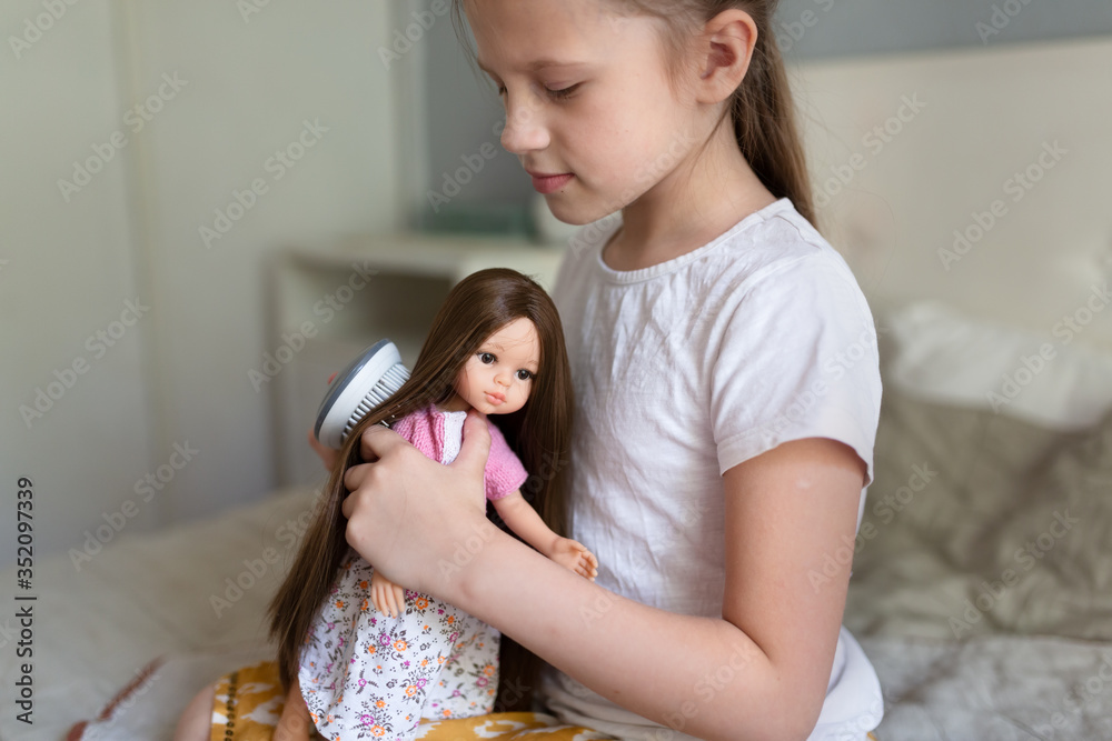 Caucasian girl combing a doll with long hair, a girl playing dolls ...