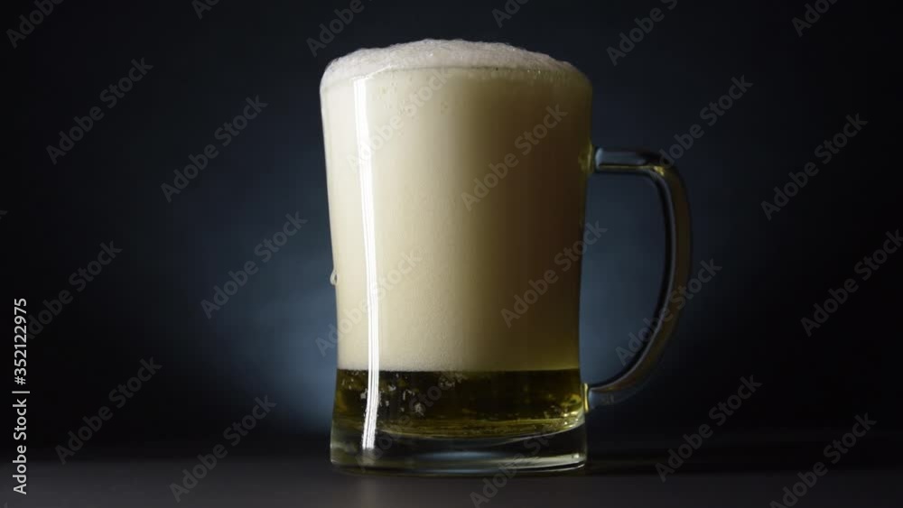 Drops of beer run down the sides of an overflowing beer mug. Slow ...