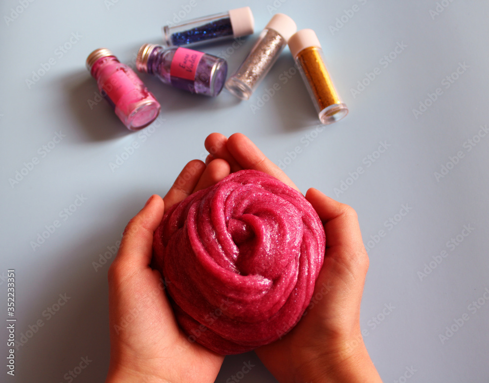 Child’s hands play with pink slime on a blue background next to small ...
