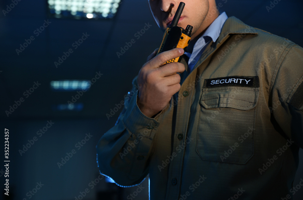 Professional security guard with portable radio set in dark room ...