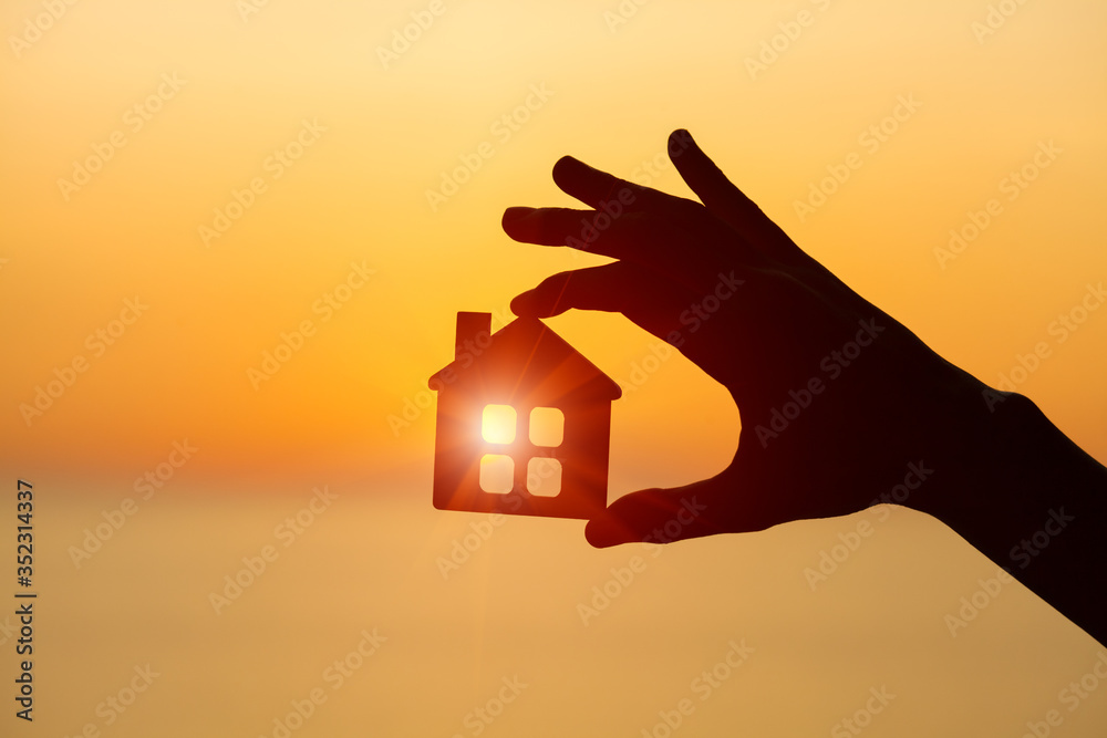 silhouette of man's hand holding small wooden house against sunset or ...