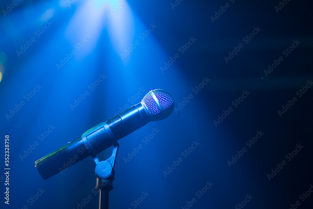 Close up on a stage microphone on a mic stand, background is a dark ...