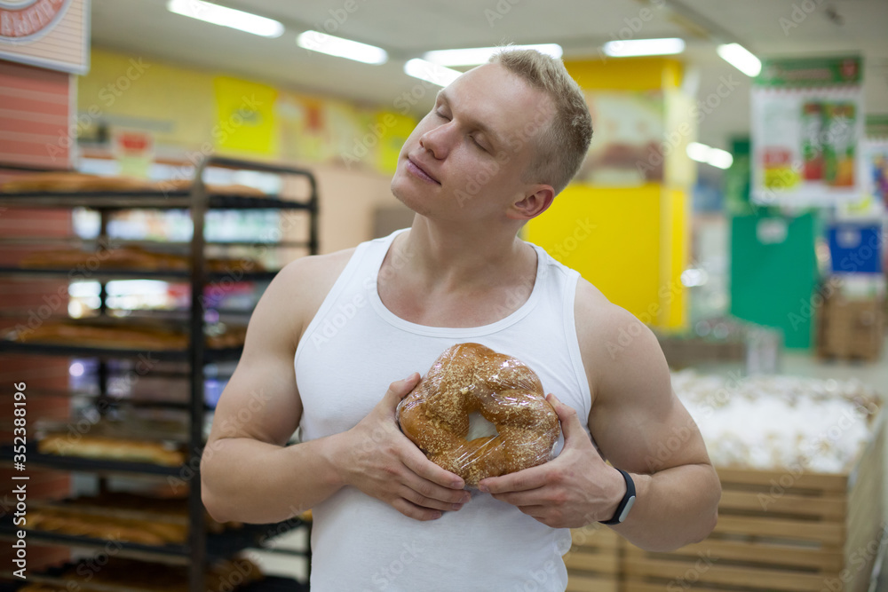 Muscular male athlete holds a loaf of bread dreamily closing his eyes ...