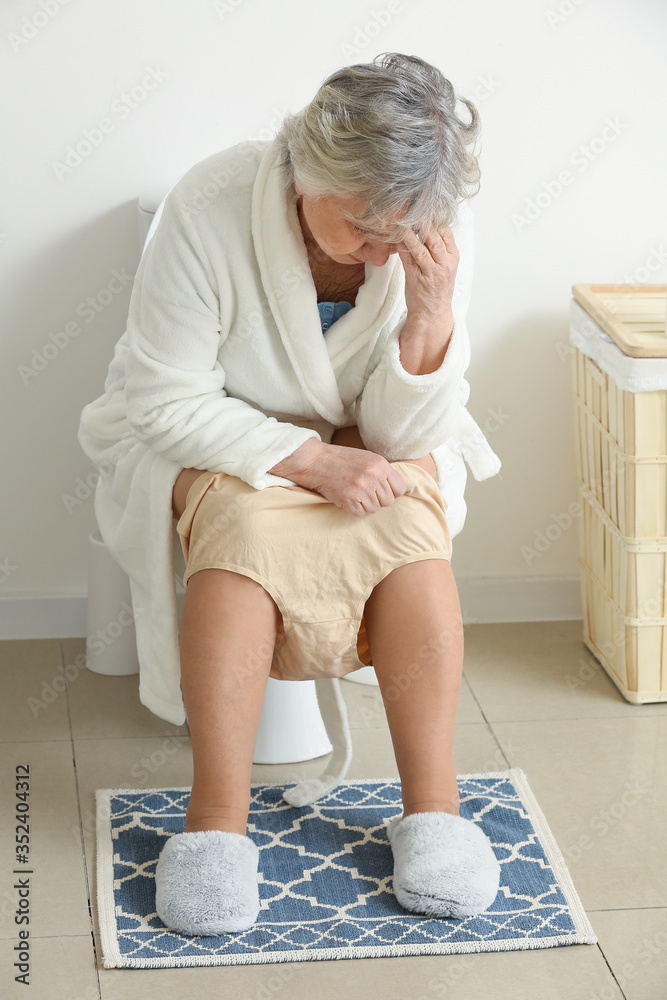 Elderly Woman With Hemorrhoids Sitting On Toilet Bowl In Restroom Stock