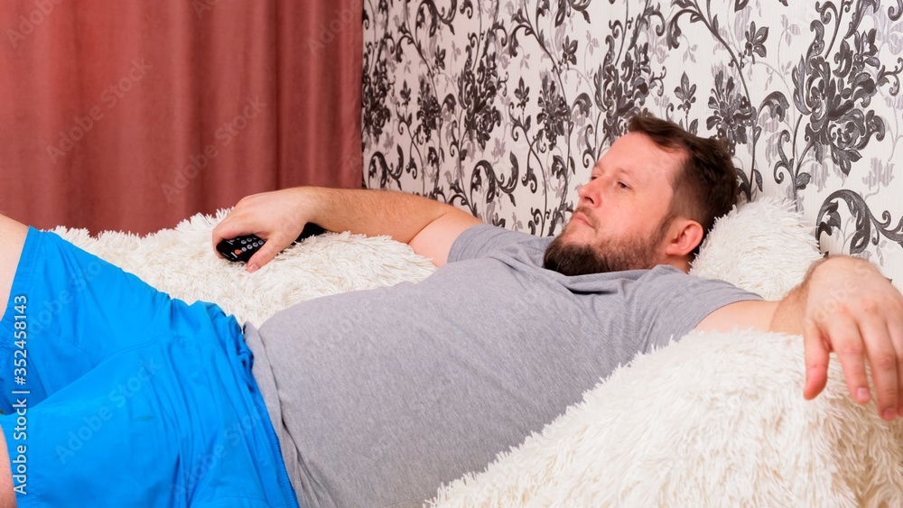 bearded handsome fat man is watching TV using the remote control to ...