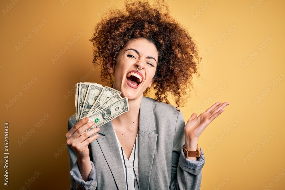 Young beautiful woman with curly hair and piercing holding dollars ...