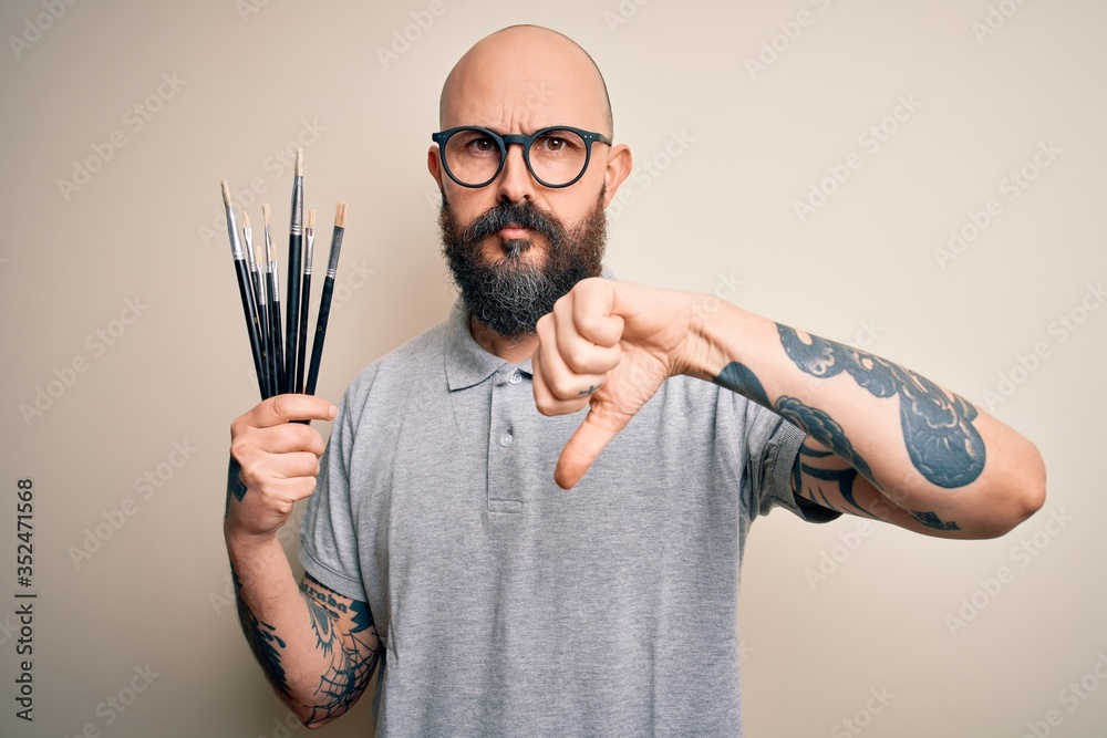 Handsome bald artist man with beard and tattoo painting using painter ...