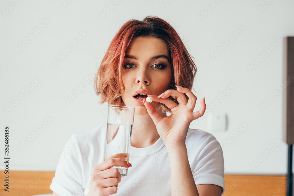 attractive girl eating pill and holding glass of water at home on self ...