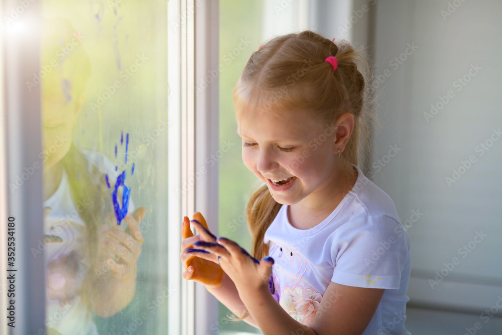 Portrait of a happy little girl draw palms on the window. Painted ...