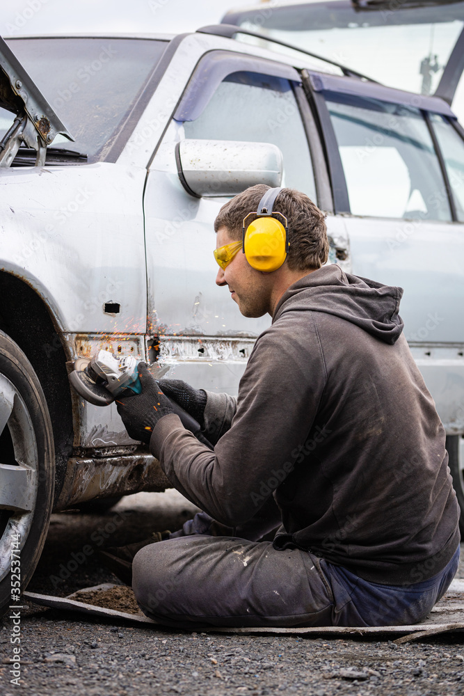 Man works as a grinder Rusty car. Preparing the surface of the car body ...