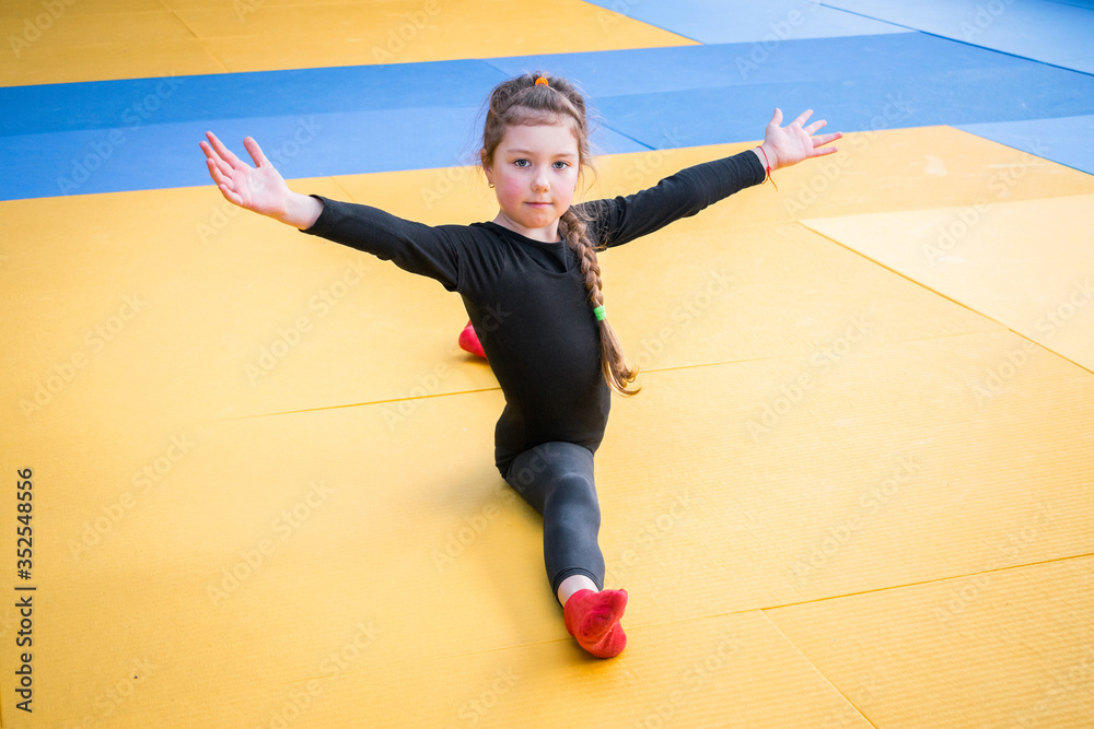 Little girl is sitting on the splits in the gym. The child does ...