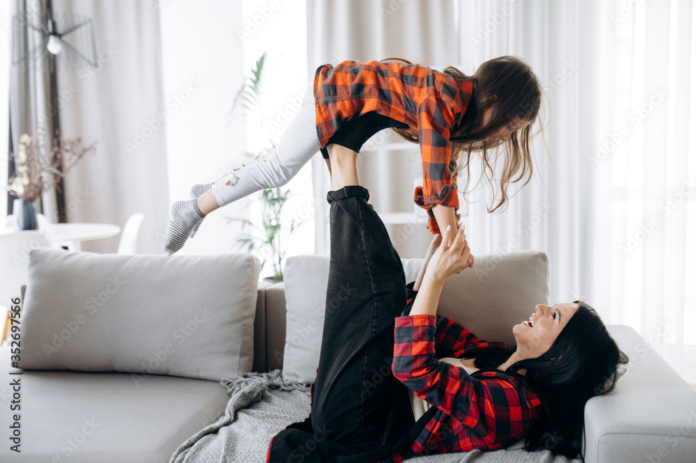 Attractive young mom having fun with their adorable little daughter, they play on a comfortable ...