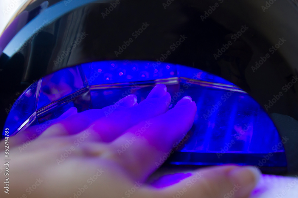 Closeup of the hand of a woman inside a UV lamp, curing her recently ...