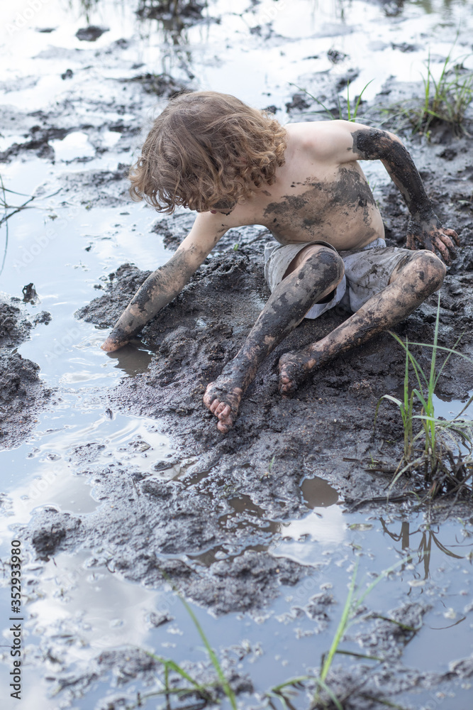 A little boy is playing in the mud. He is covered in dirt and mud ...