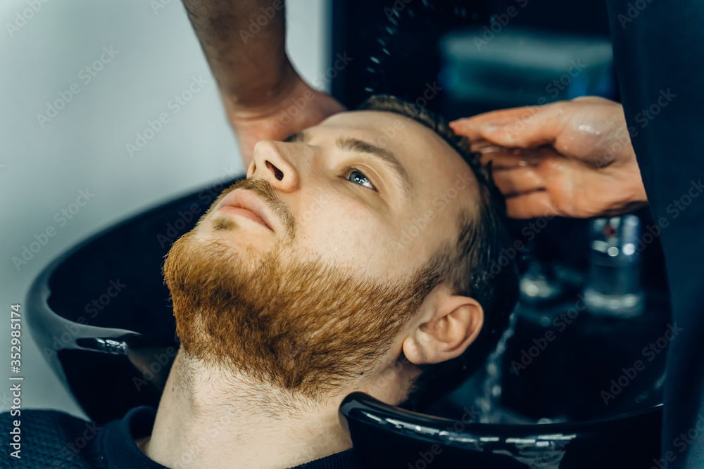 Attractive male is getting a modern haircut in barber shop. Top view of ...