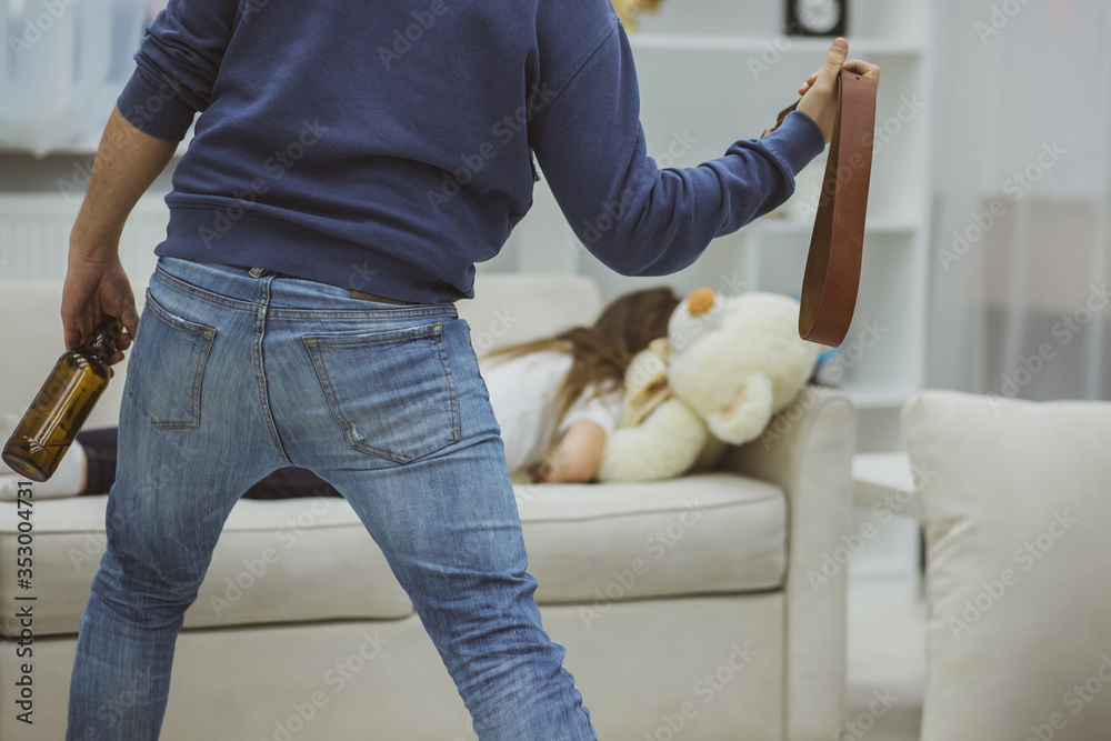 Cropped view of father holding belt and scared daughter hiding on the ...