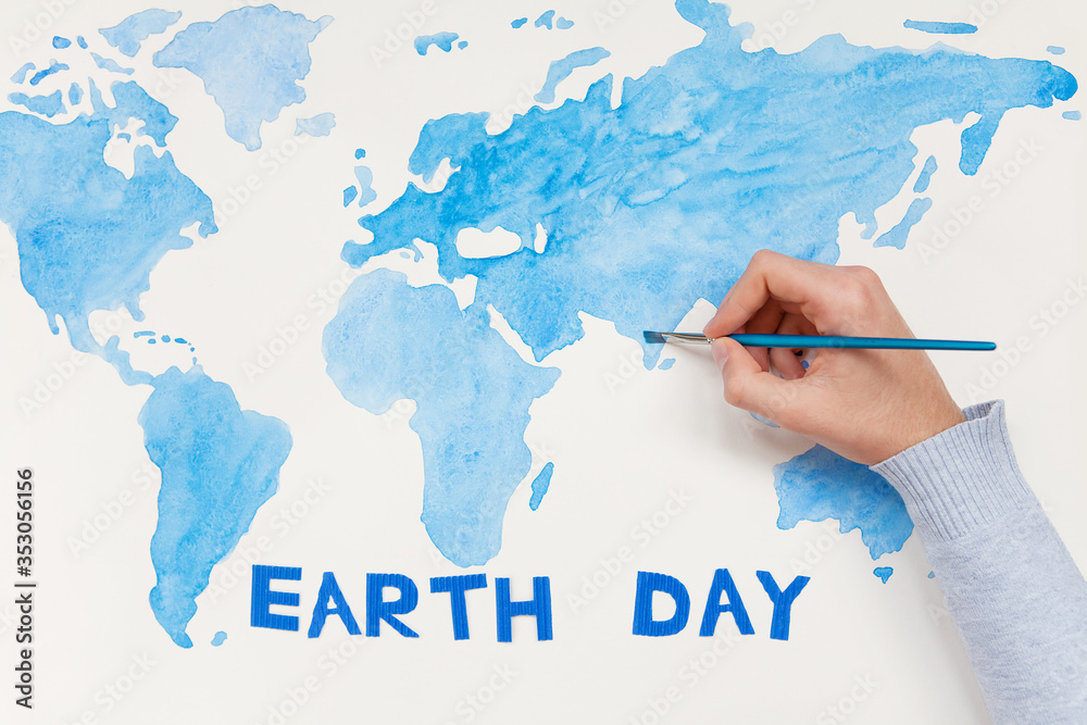 Human hand draws watercolor world map with brush. Earth Day text ...