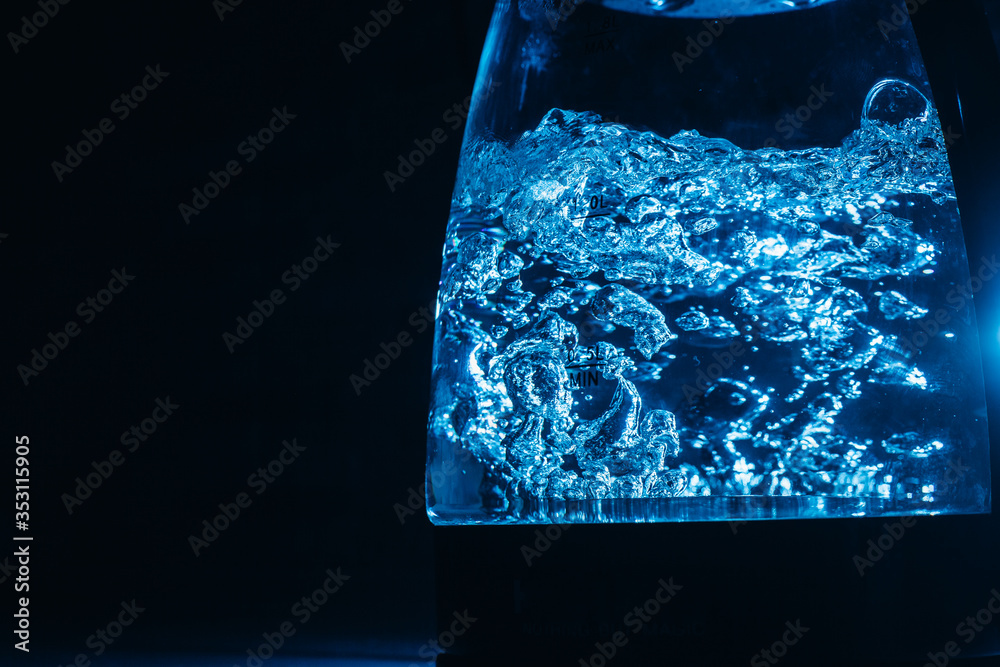 Boiling glass black teapot with blue backlight on a black background ...