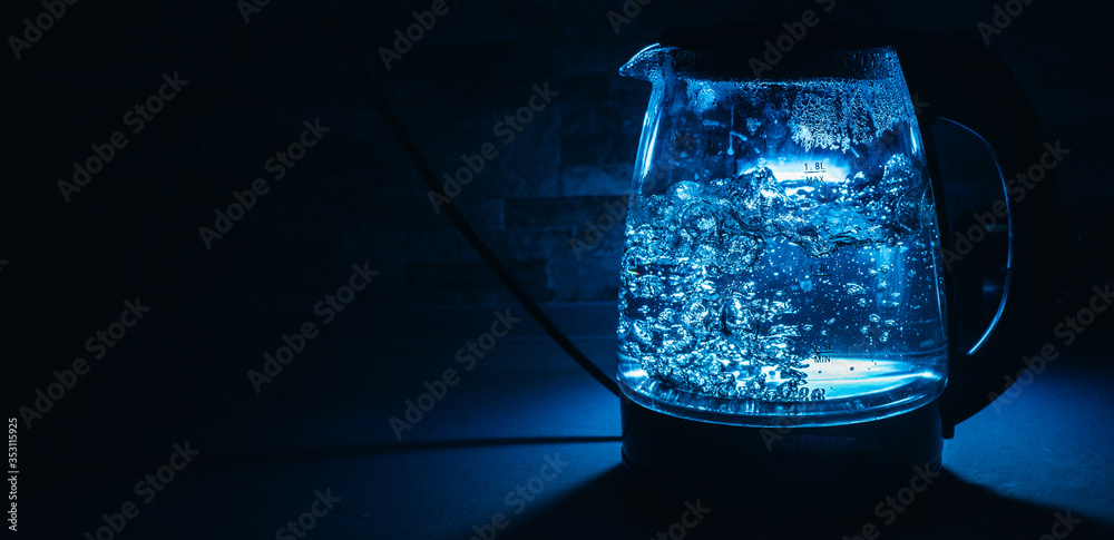 Boiling glass black teapot with blue backlight on a black background ...