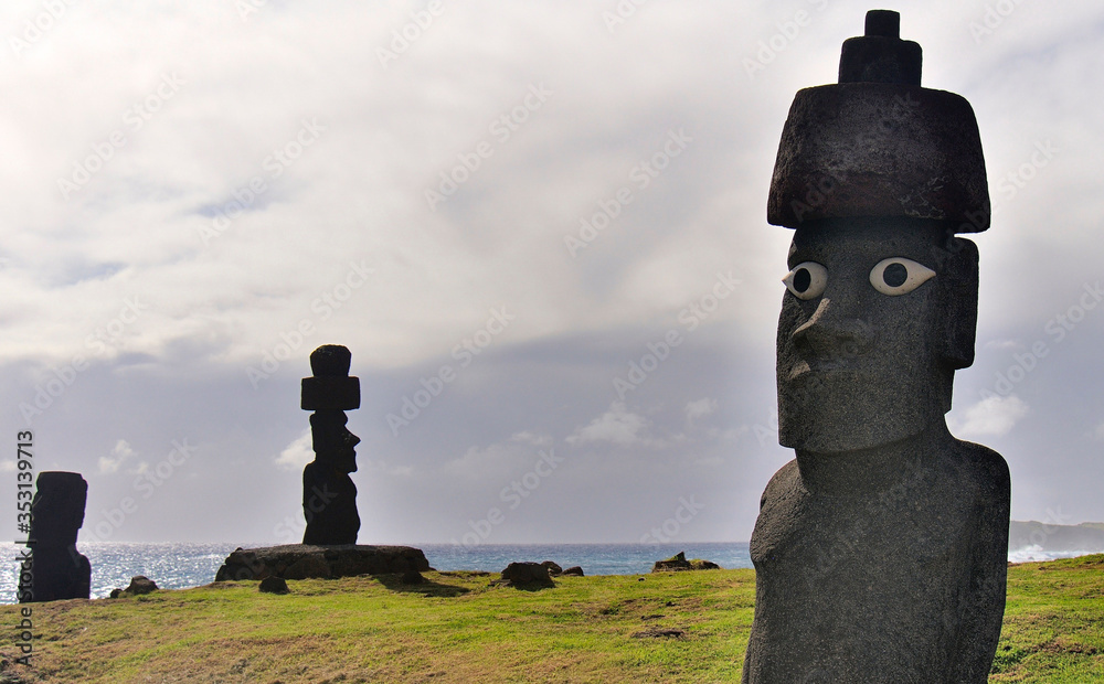 Three Moai statues of Ahu Tongariki against a cloudy sky, green grass ...