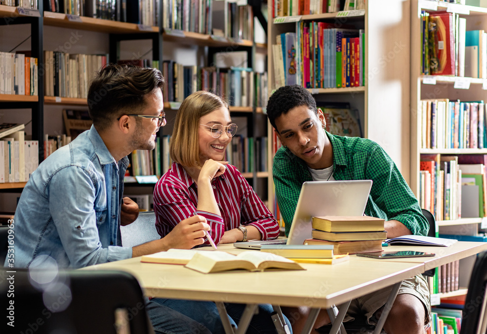 Three young students study in the school library, they using laptop for ...