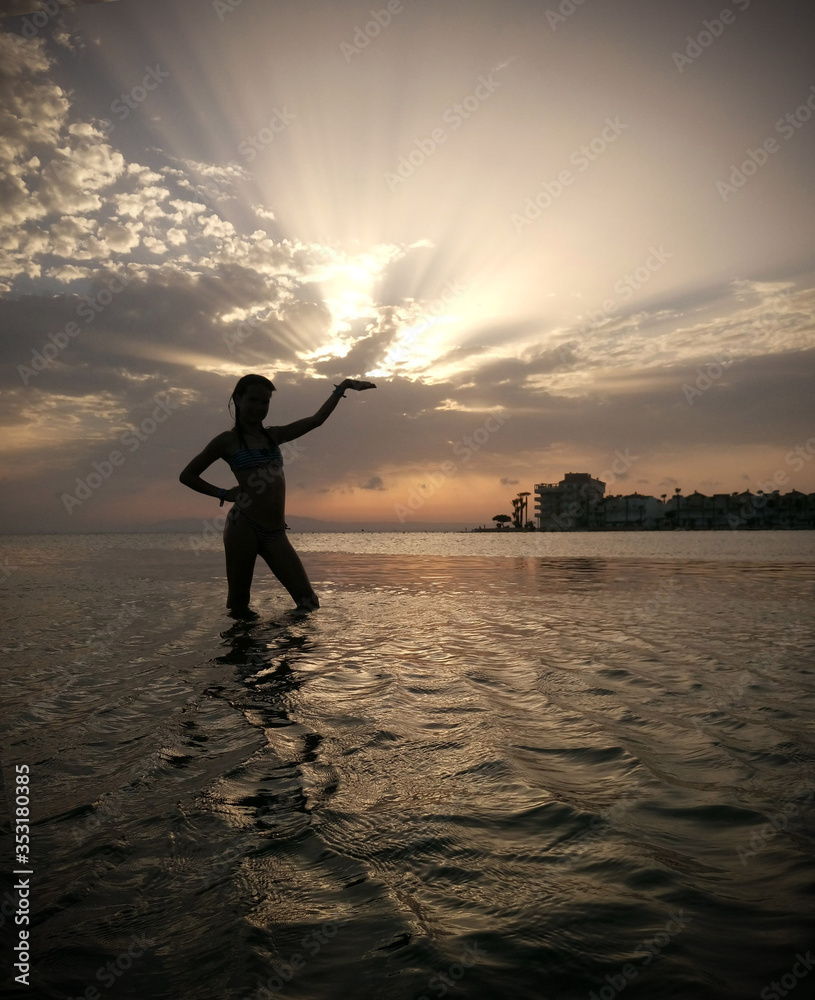 Silhouette of little girl trying to catch sun during sunset at sea on ...