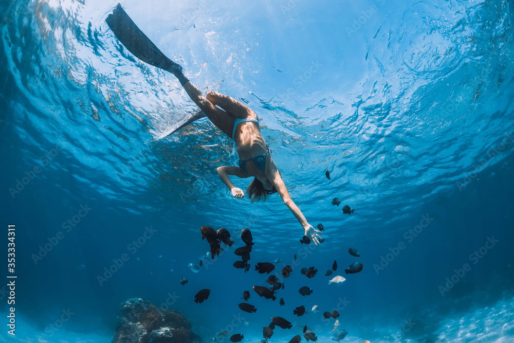 Freediver girl in bikini with fins glides underwater in blue ...