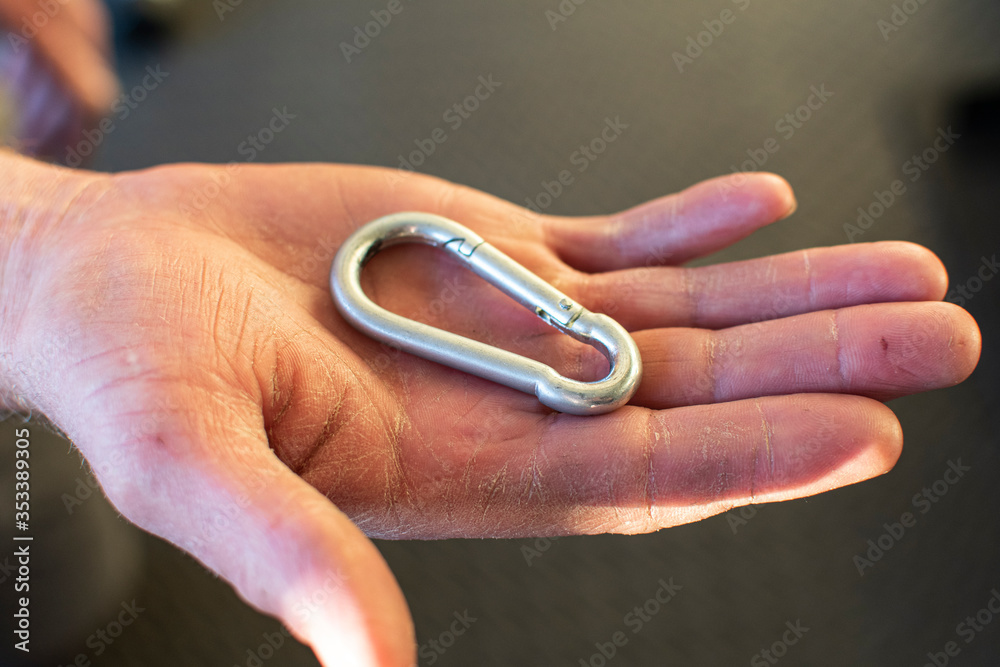 Carabiner climbing clip in the palm of a climber with worn rough skin ...