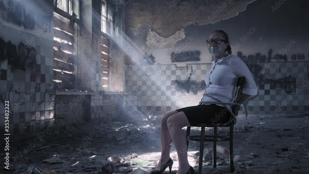 Kidnapped woman looks around in abandoned building while sitting tied ...
