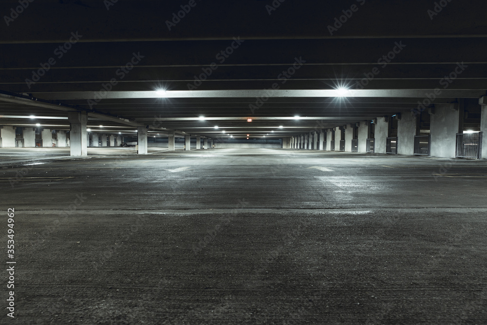 Grungy, dimly lit empty parking garage with overhead lights and an exit ...