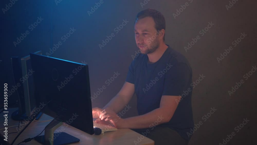 Man geek hacker is working at computer in dark underground office room ...