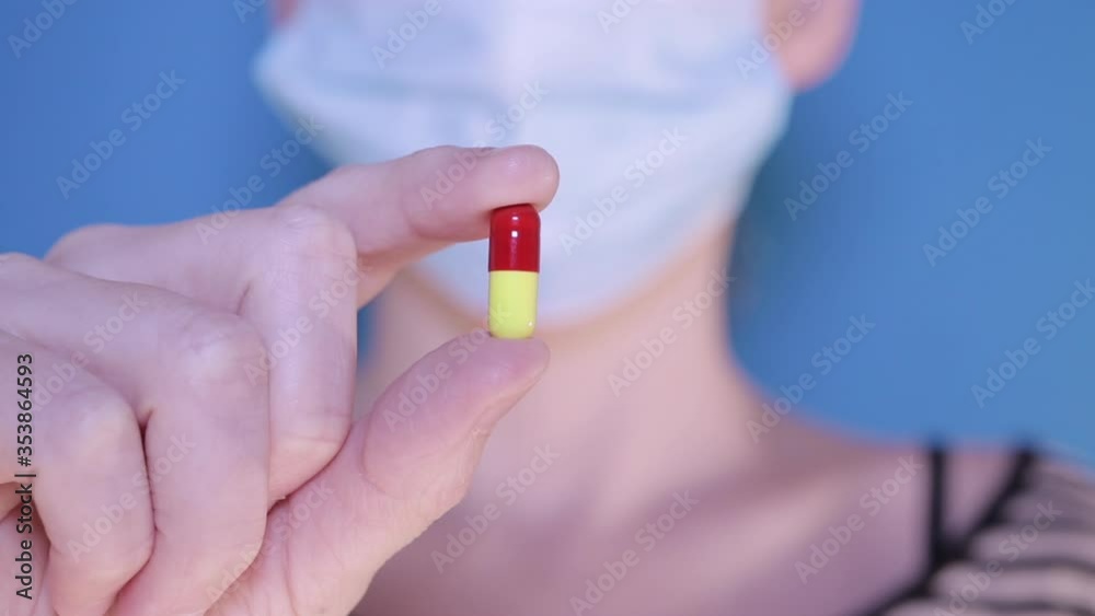 Person in a face mask holding up a medicine pill, closeup with a ...