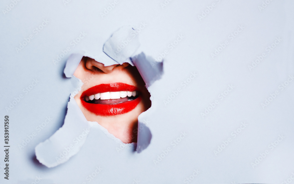 Smile of a beautiful girl, with red lips through torn paper. Fashion ...