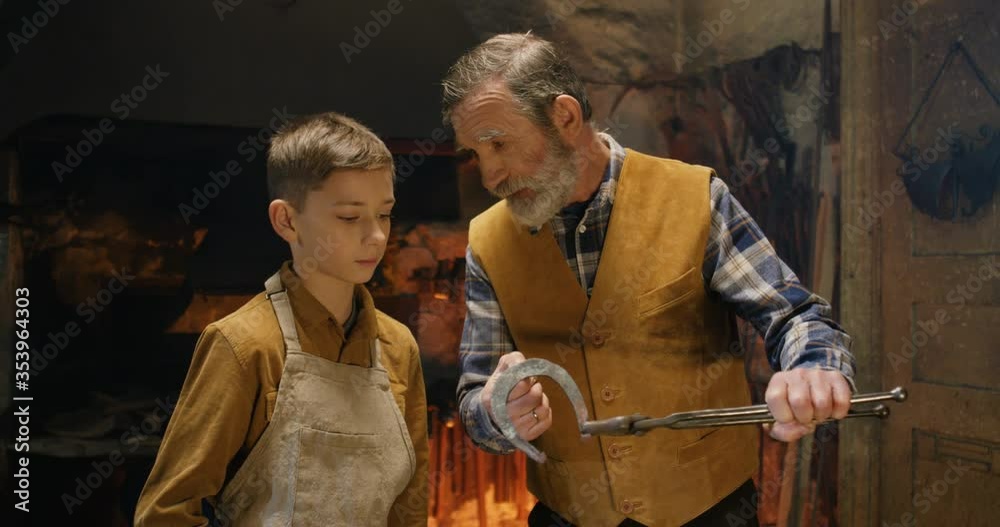 Caucasian senior grandfather blacksmith talking with cute teen grandson ...