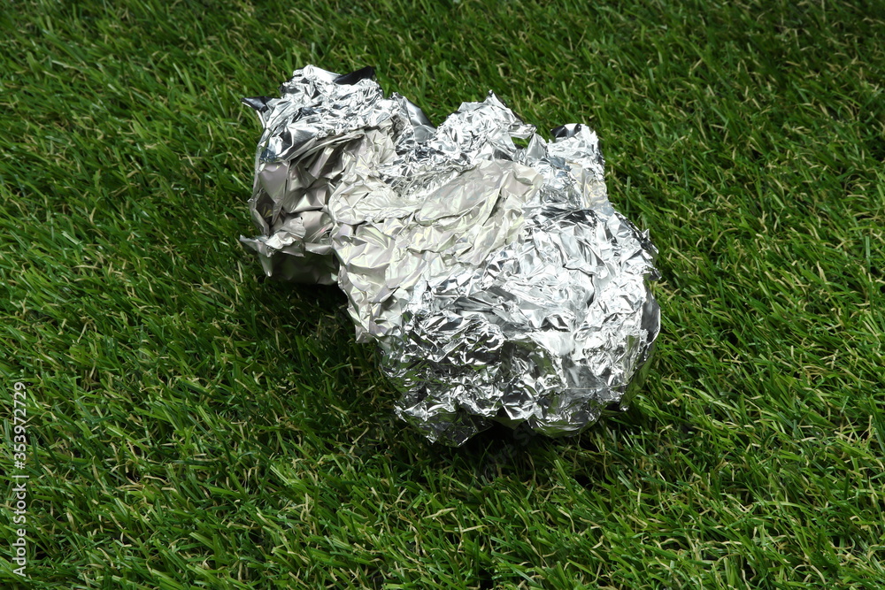 Aluminium foil leftover on the green grass field. Bad behavior concept ...