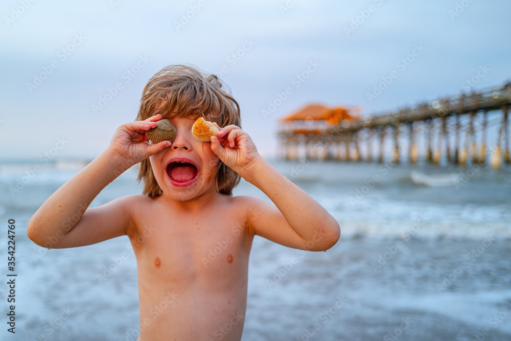Funny little boy with shell on sea. Cute kid is playing with shell at ...