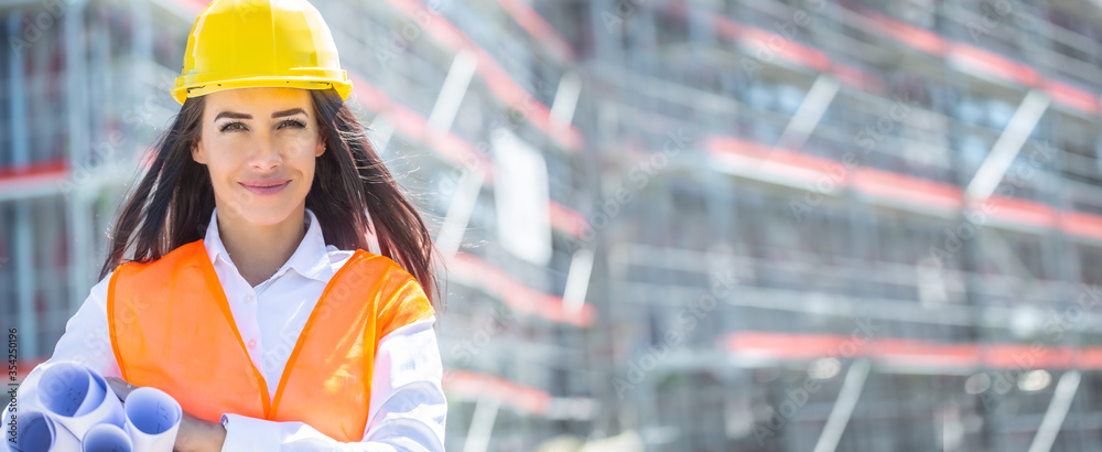Female architect wearing orange safety vest and a yellow helmet holds ...