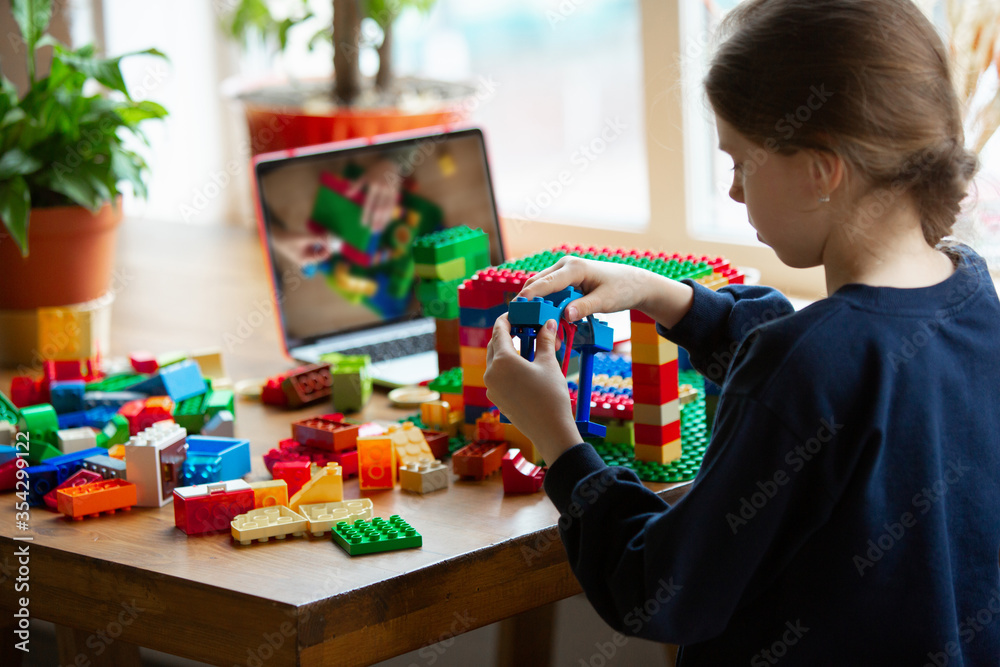 Girl playing with constructor at home, watching teacher's online ...