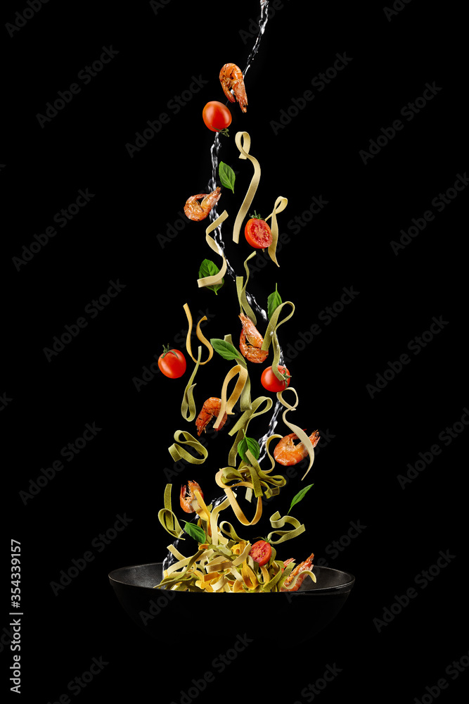 Wok pan, falling pasta with tomatoes, shrimps and green basil against ...
